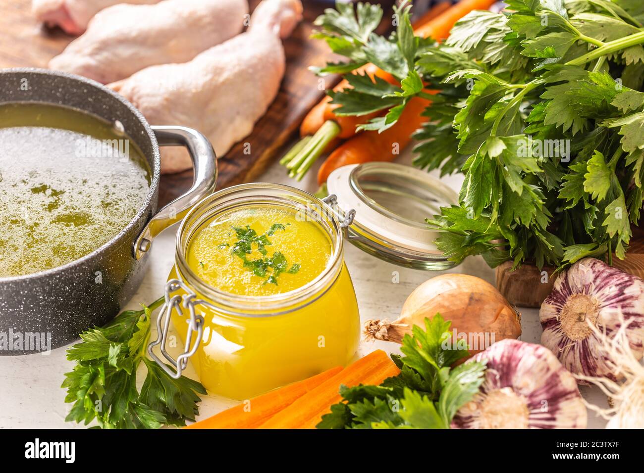 Chicken broth in a glass jar raw chicken legs carrot onion celery herbs ...