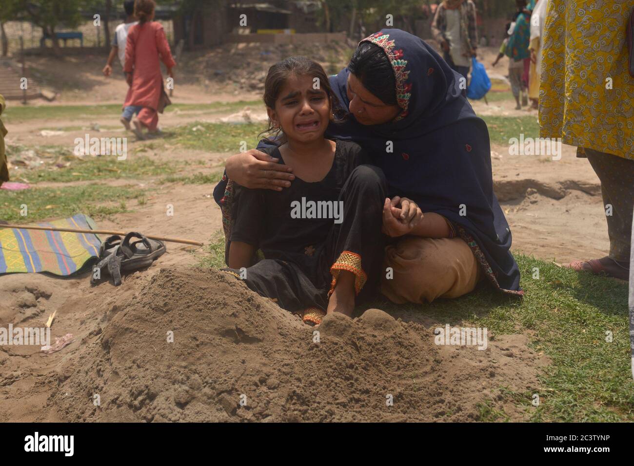 Pakistani people pray around an ailing child partially buried in mud at ...