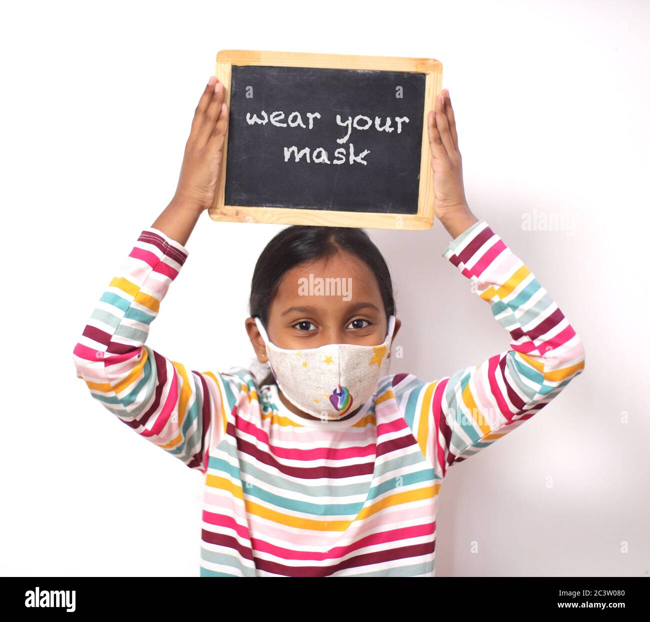 Child girl wearing face mask holding chalk board saying "wear your mask ...
