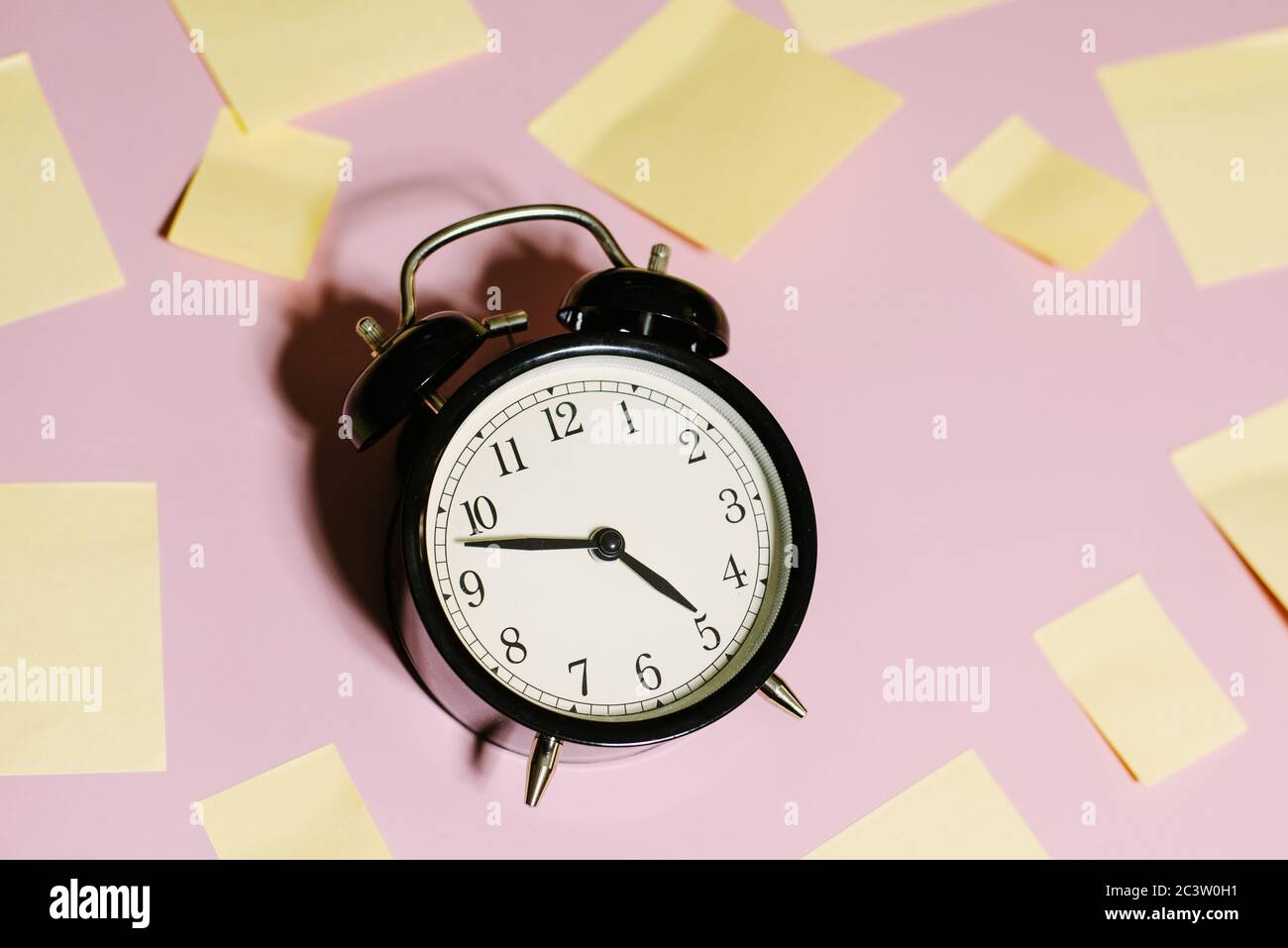 White alarm clock and yellow sticky notes on a pink background. The ...