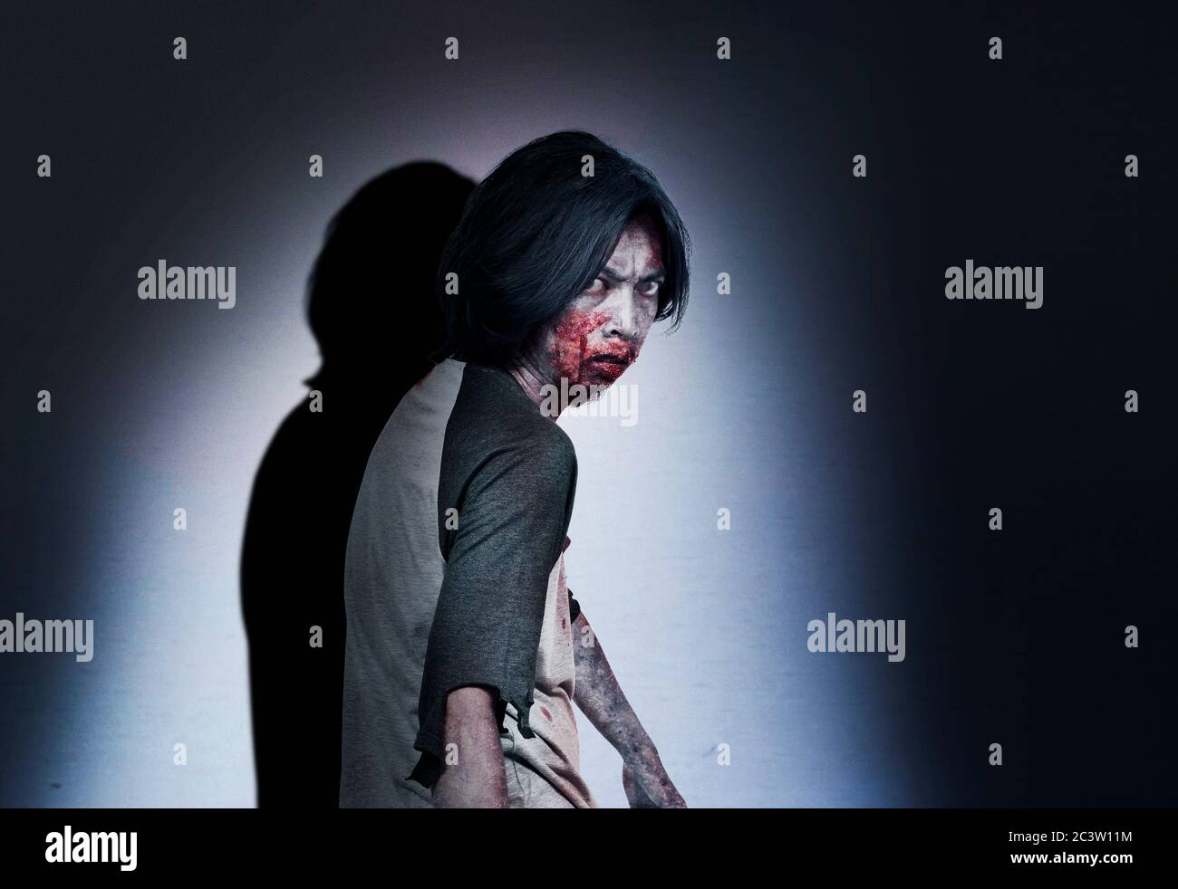 Scary zombie with blood and wound on his body standing on the dark room ...