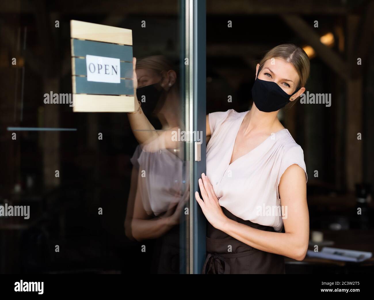 Portrait of waitress with face mask standing at the door in restaurant ...