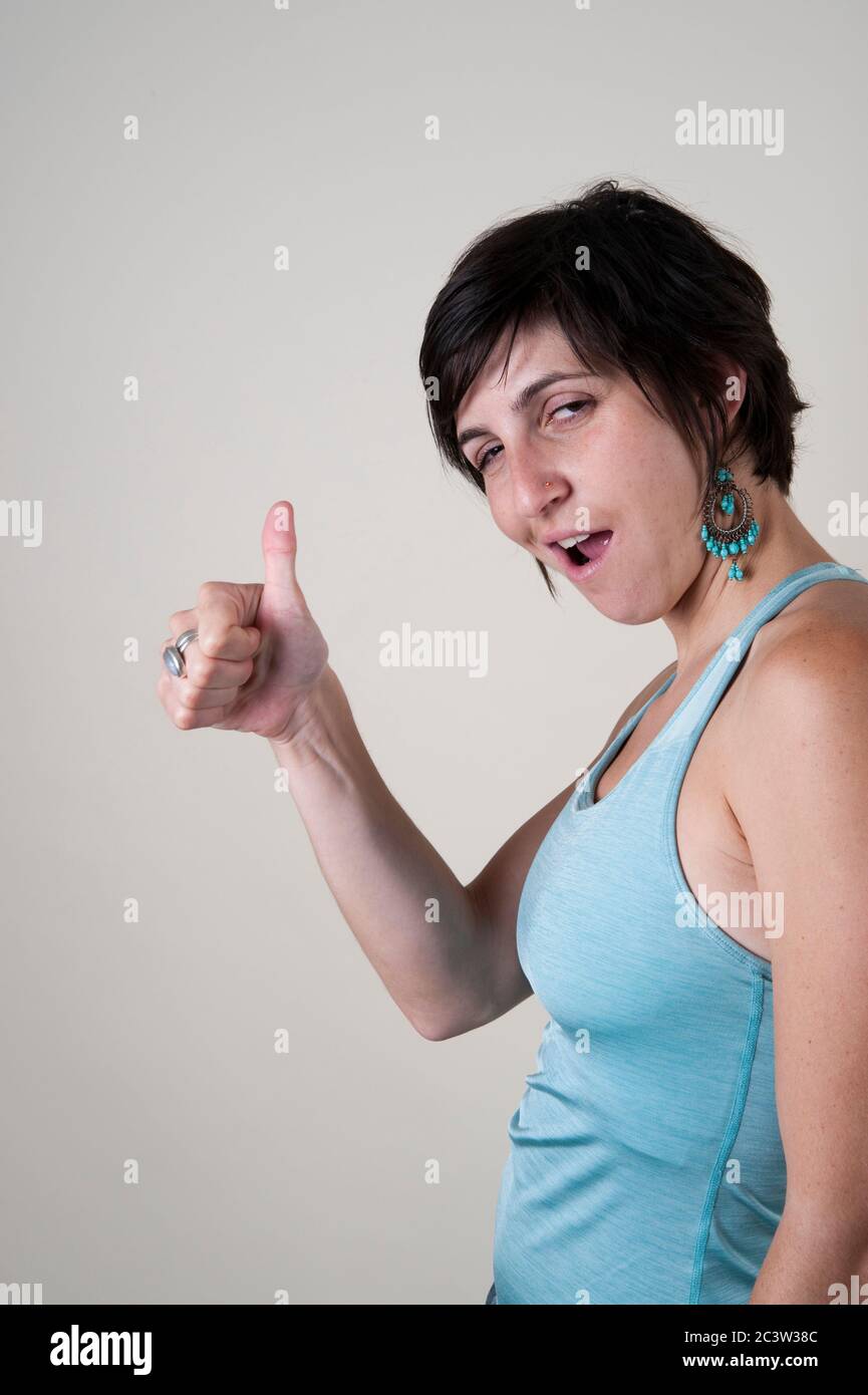 Studio shot of a smiling female model in her 20s gives the thumbs up on ...