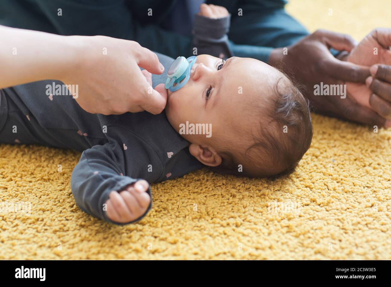 Portrait of cute mixed-race baby lying on yellow carpet at home with ...