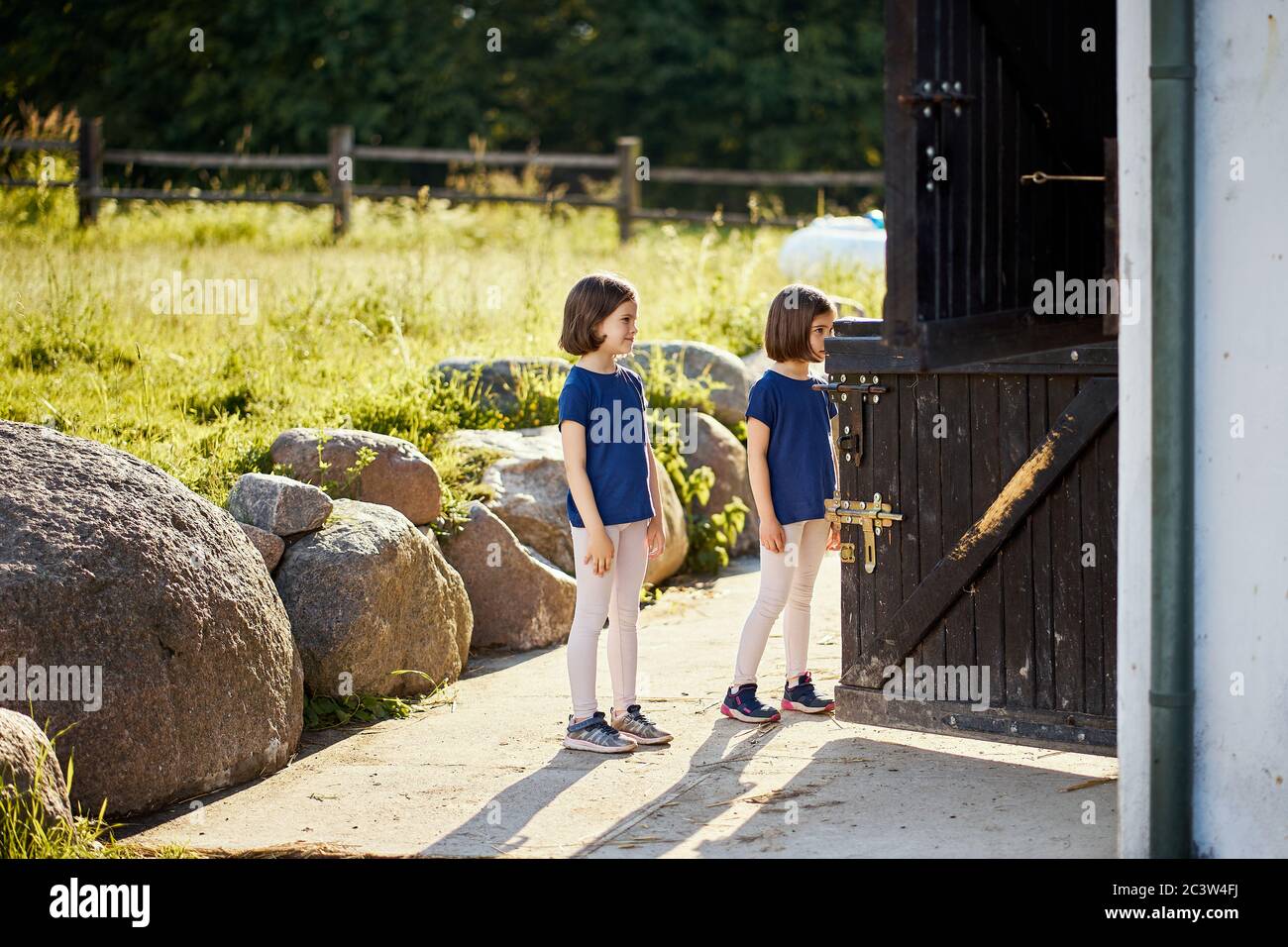 two girls are standing in front of the stable in the summer Stock Photo ...