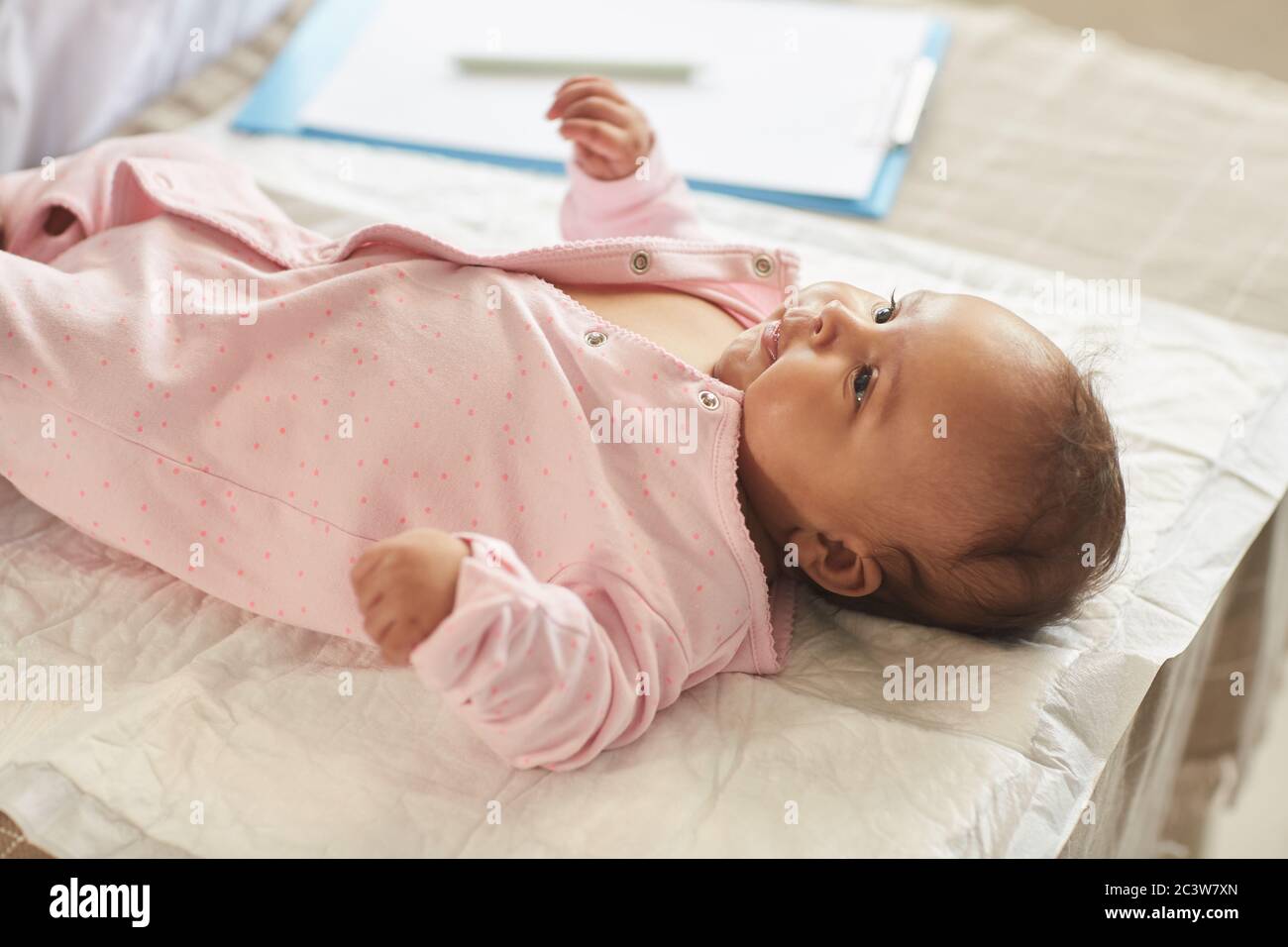 Warm-toned portrait of cute baby girl lying on changing table at ...