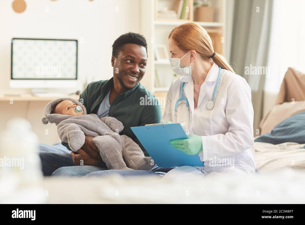 Portrait of smiling African-American dad holding baby and listening to ...