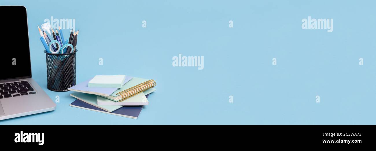 Laptop, stack of notepads, stand with stationery on a blue background ...