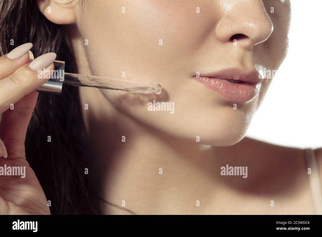 Close up beautiful young woman applying serum, oil on face on white ...