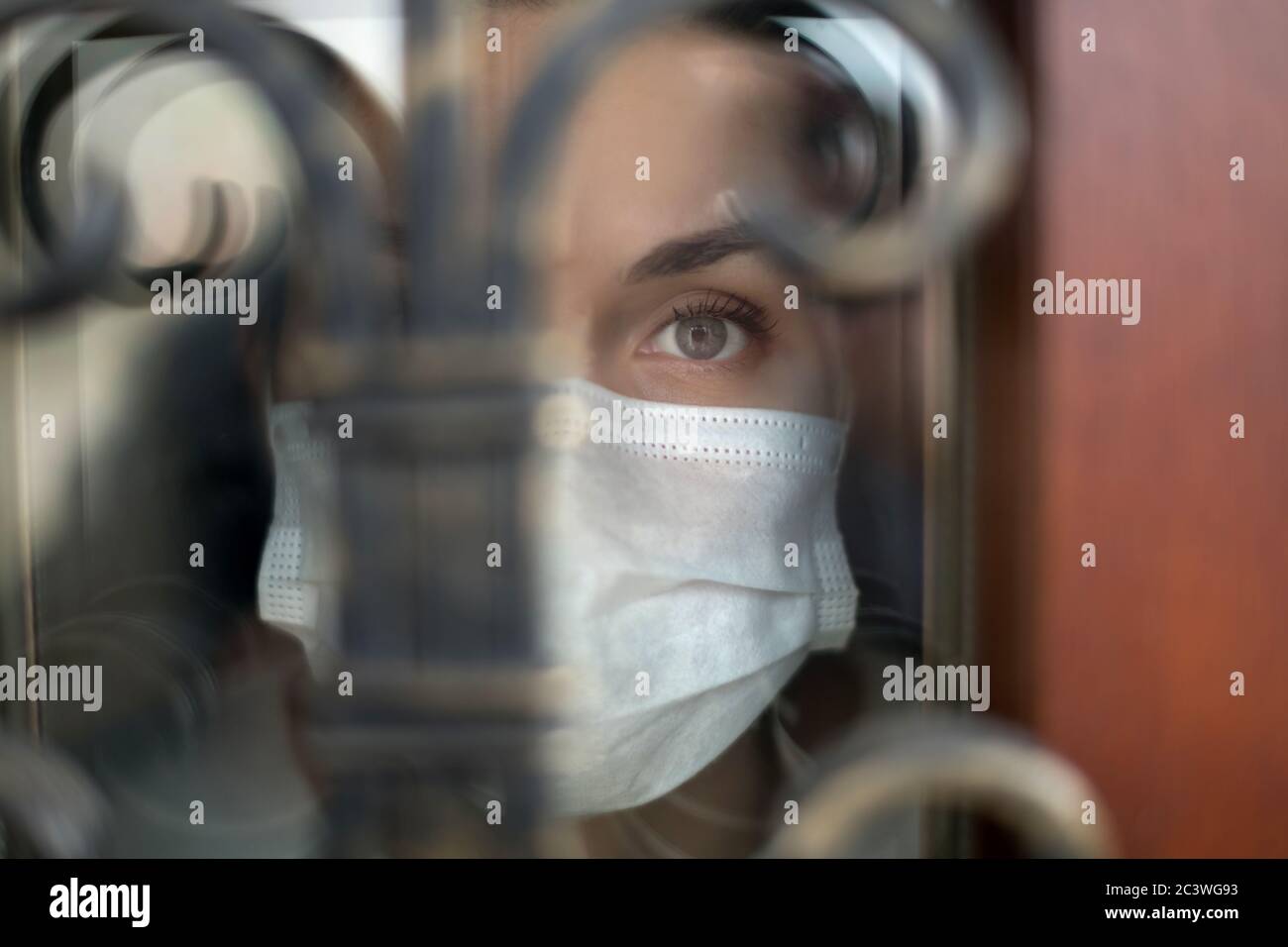 Cold look of a girl through the front door of a house during quarantine ...