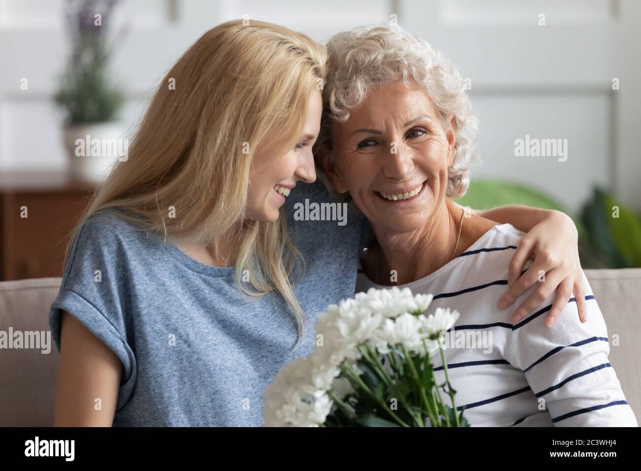 Grownup daughter elderly mom hugging sitting on couch with flowers Stock Photo - Alamy