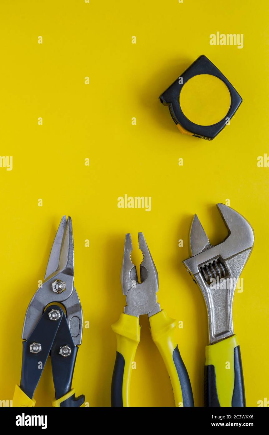Line of hand tools with black and yellow handles on a yellow background ...