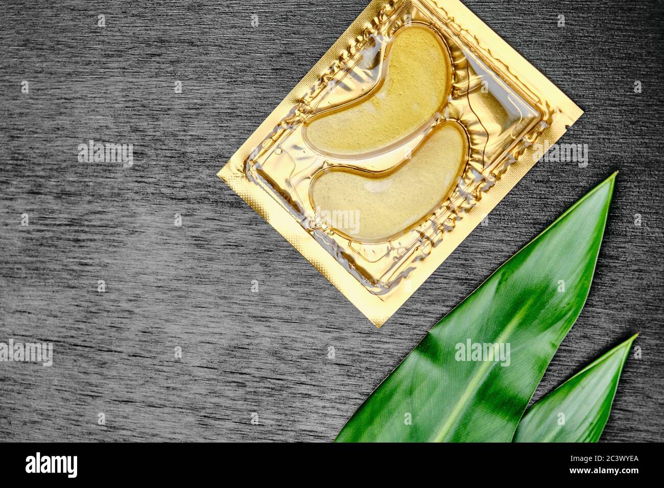 Gold cosmetics hydrogel patches and green leaves on a black wooden ...