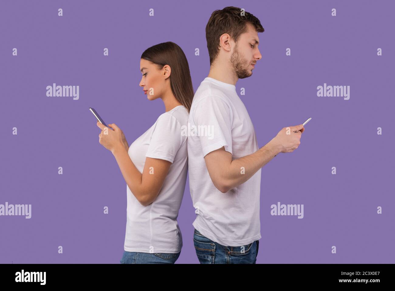 Portrait of young couple standing back to back using phones Stock Photo ...