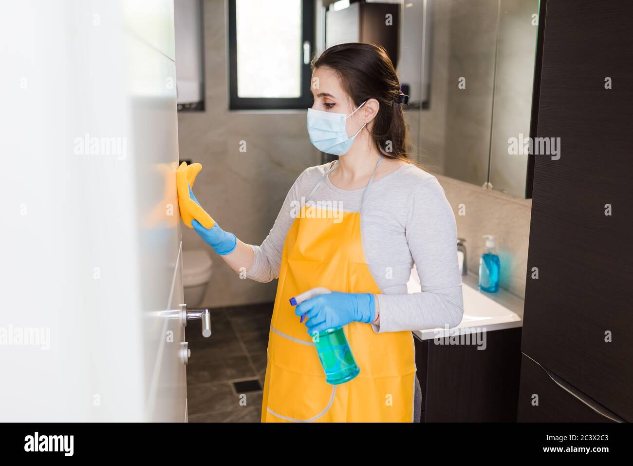 Woman housekeeper wipes the door with rag and using spray disinfectant ...
