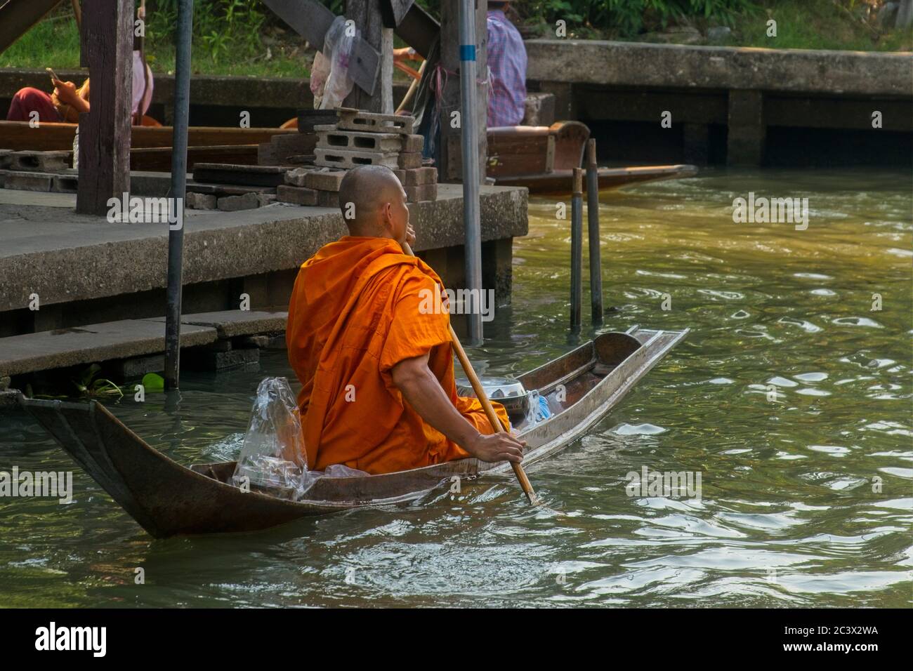 Bhudist monks and locals at Bangkok's floating market. A Monk paddling ...