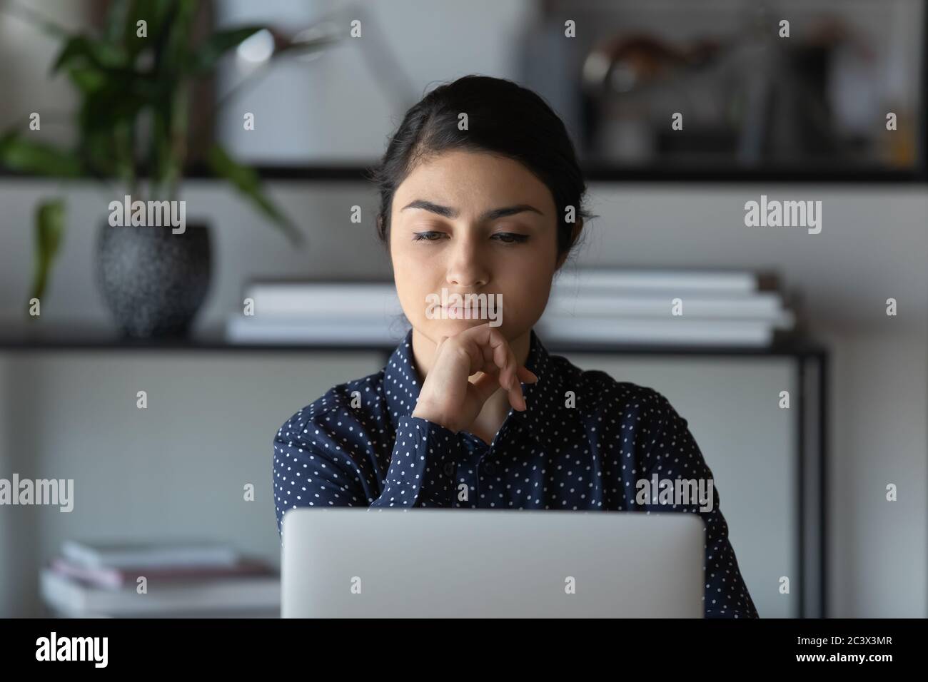 Indian employee looking at laptop screen thinking over problem solution ...
