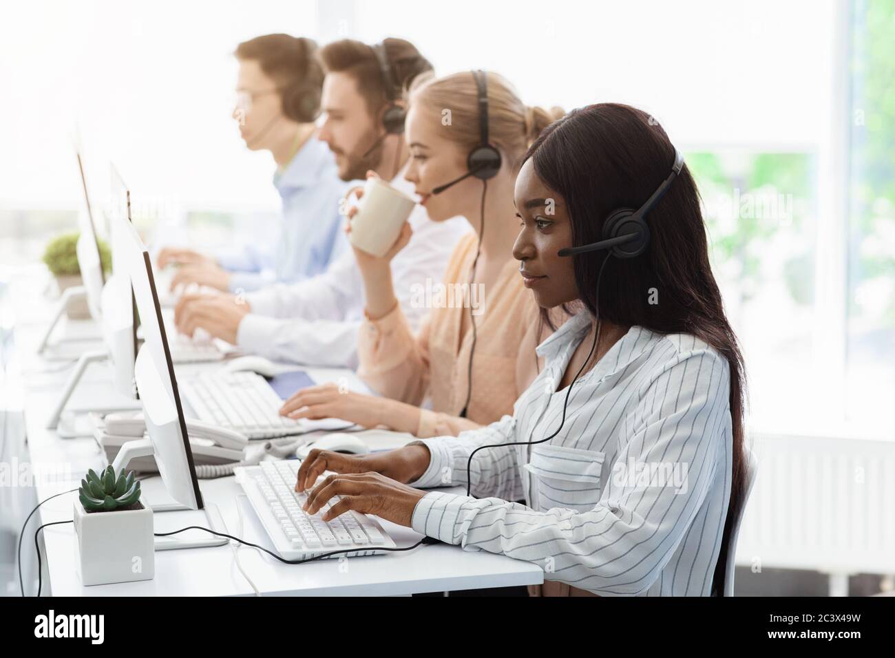 Line of call centre employees with headphones working on computers in ...