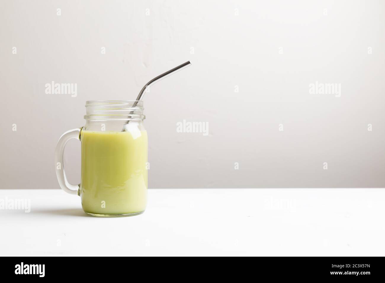 Matcha green tea latte in glass jar with metal tube on white background ...