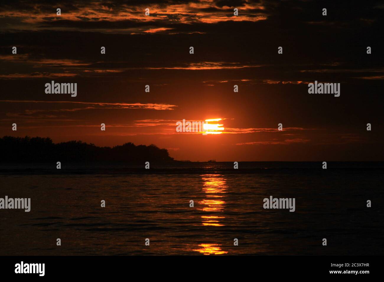 Deep red sunset with sun going down from behind clouds and light ...