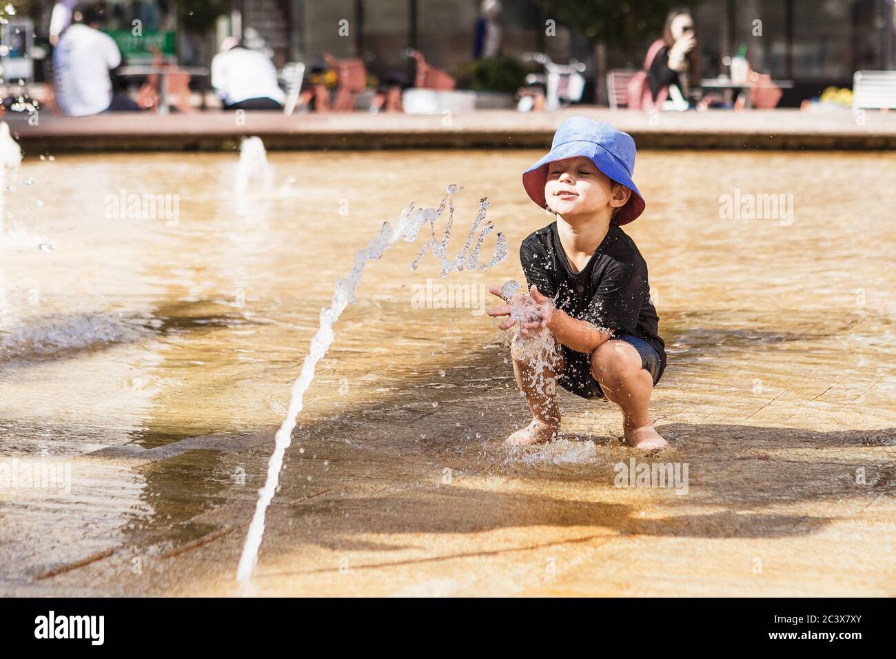 Cute little boy playing with water jet in fountain on a heat summer day ...