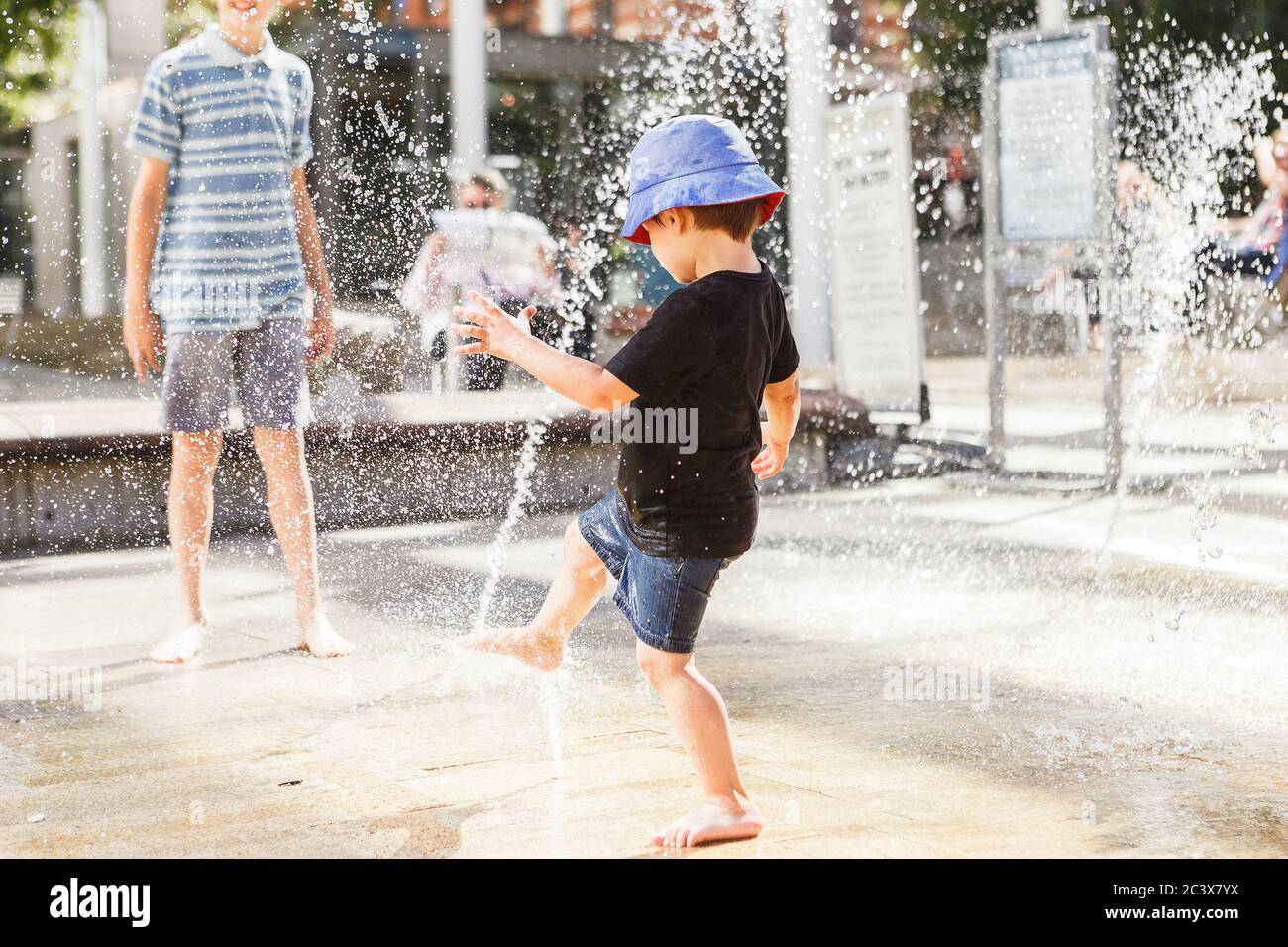 Cute little boy playing with water jet in fountain on a heat summer day ...