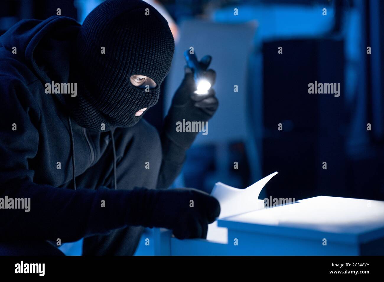 Masked thief holding and reading confidential documents Stock Photo - Alamy