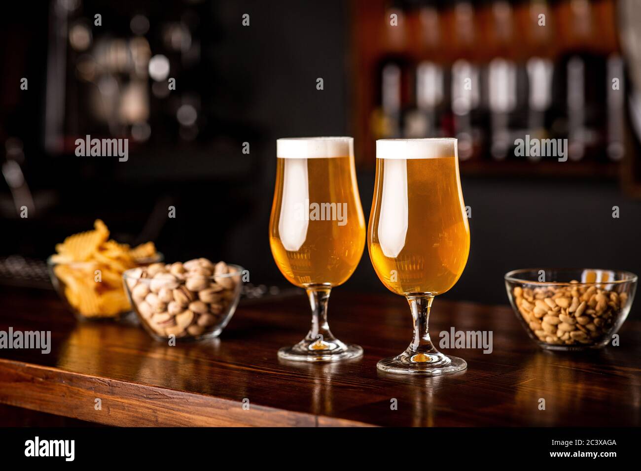 Snacks in pub on wooden bar. Two glasses with beer, chips, nuts and ...