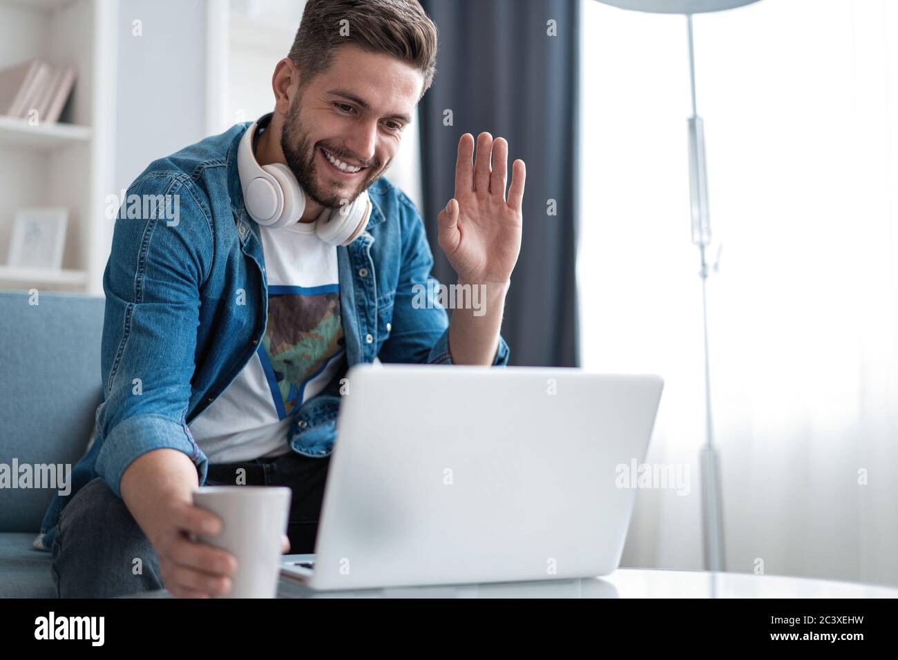 Smiling young man making video call with friends at his modern home ...
