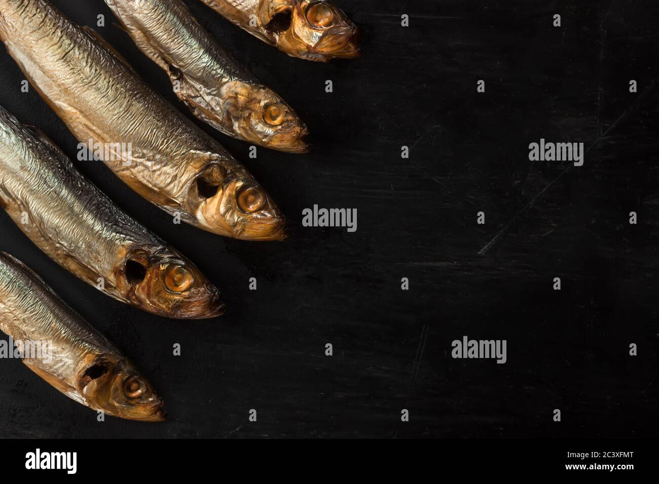 Smoked sprat fish golden brown on a black background with space for ...