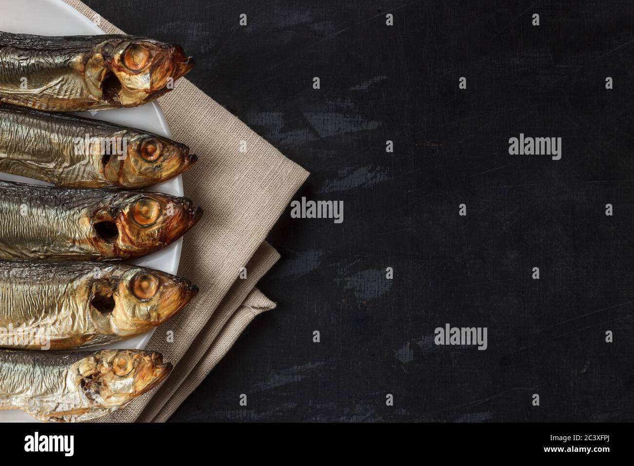 Smoked sprat fish on a plate and napkin on a black background with a ...