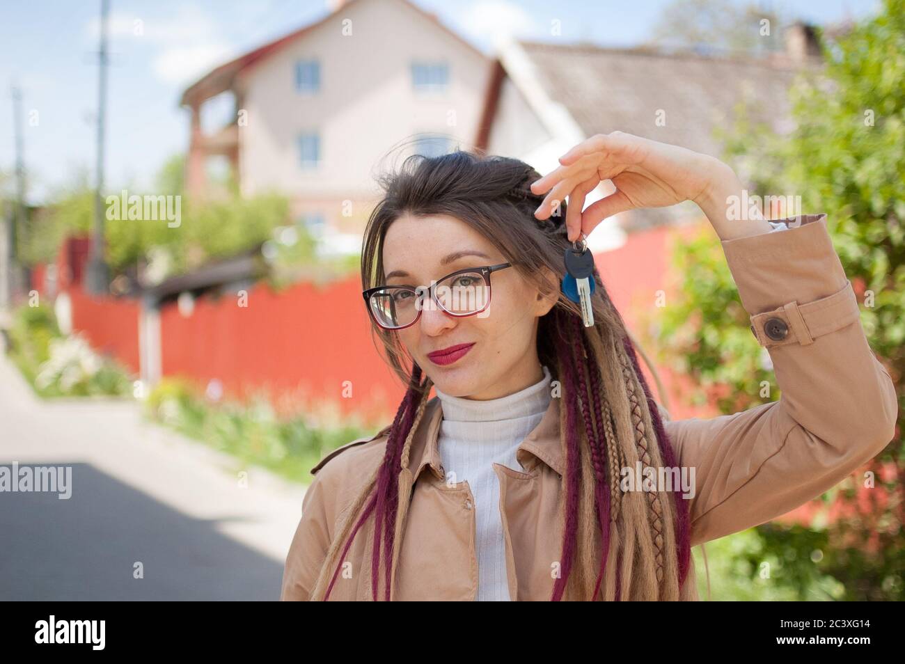 Modern young girl with long dreadlocks and eyeglasses is showing bunch ...
