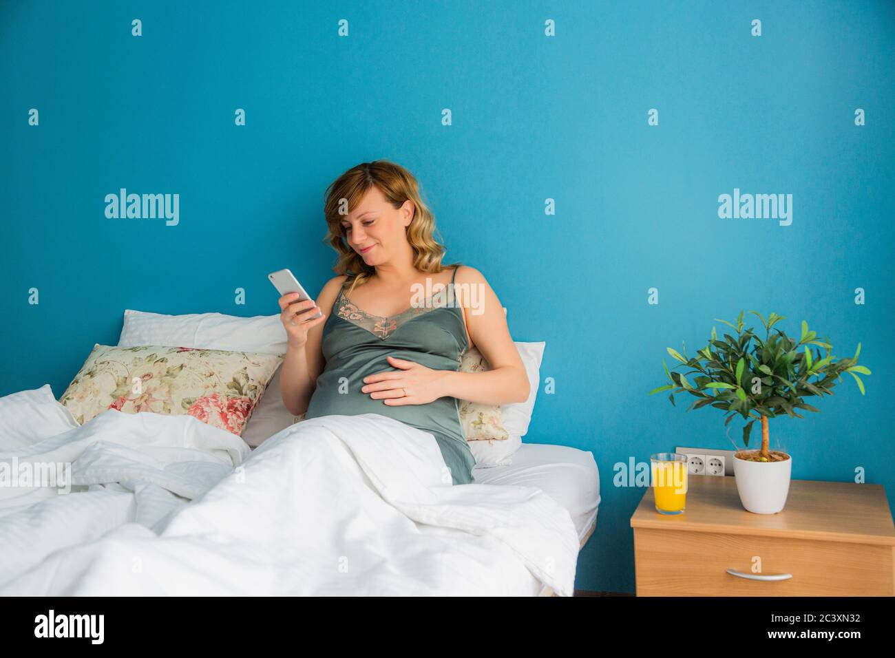 A pregnant woman in a semi-sitting position in her bed using a mobile ...