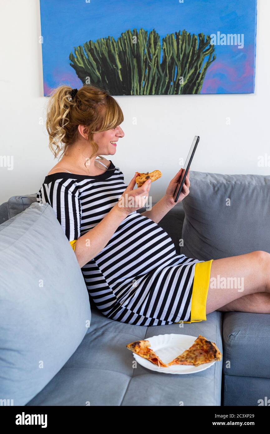 A pregnant woman in a semi-sitting position on the couch and reading ...