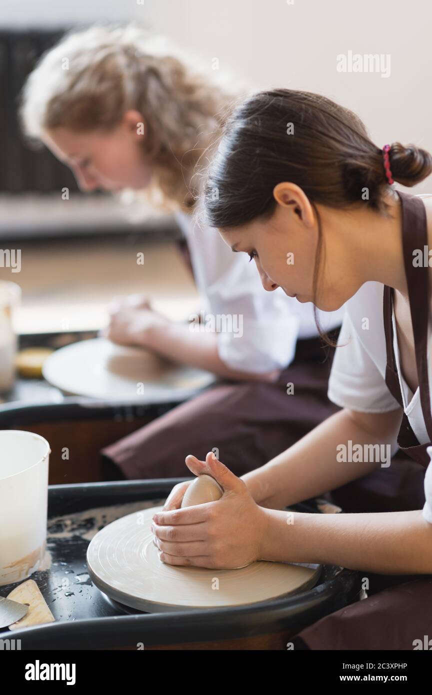 Two women make pottery on a pottery wheels, shaping clay by their hands ...