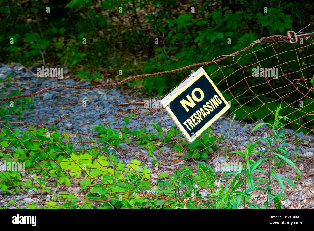 A yellow and black No Tresspassing sign hangs askew on rusted metal ...