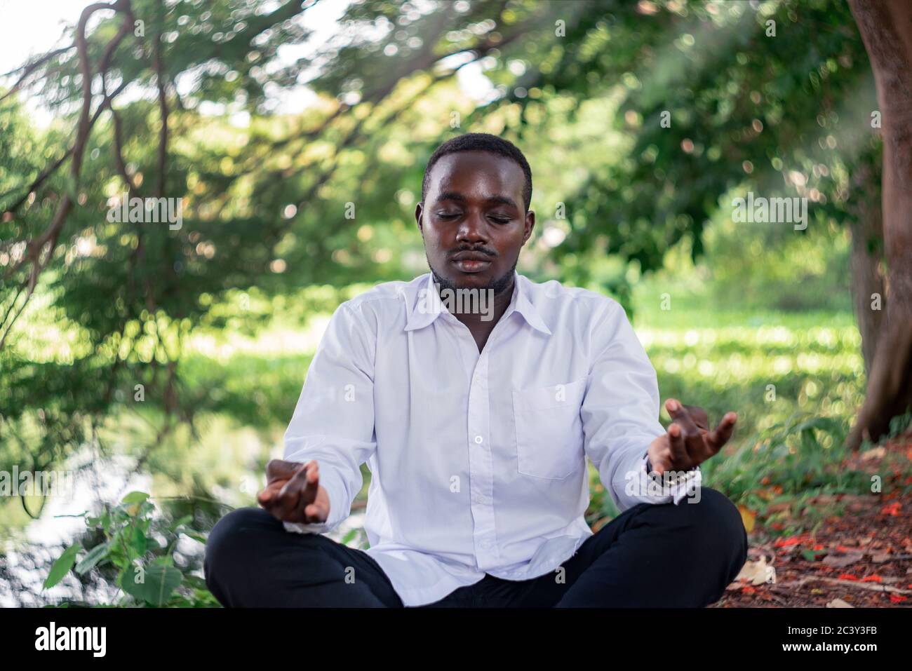 African man is sitting and meditating in green nature park Stock Photo ...