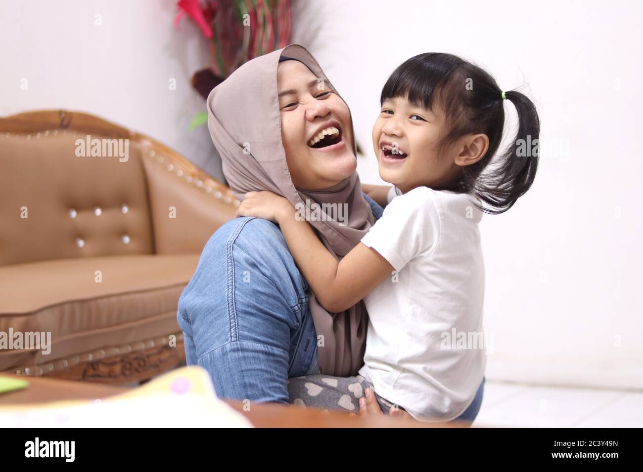 Muslim mother wearing hijab smiling while playing with her baby girl ...