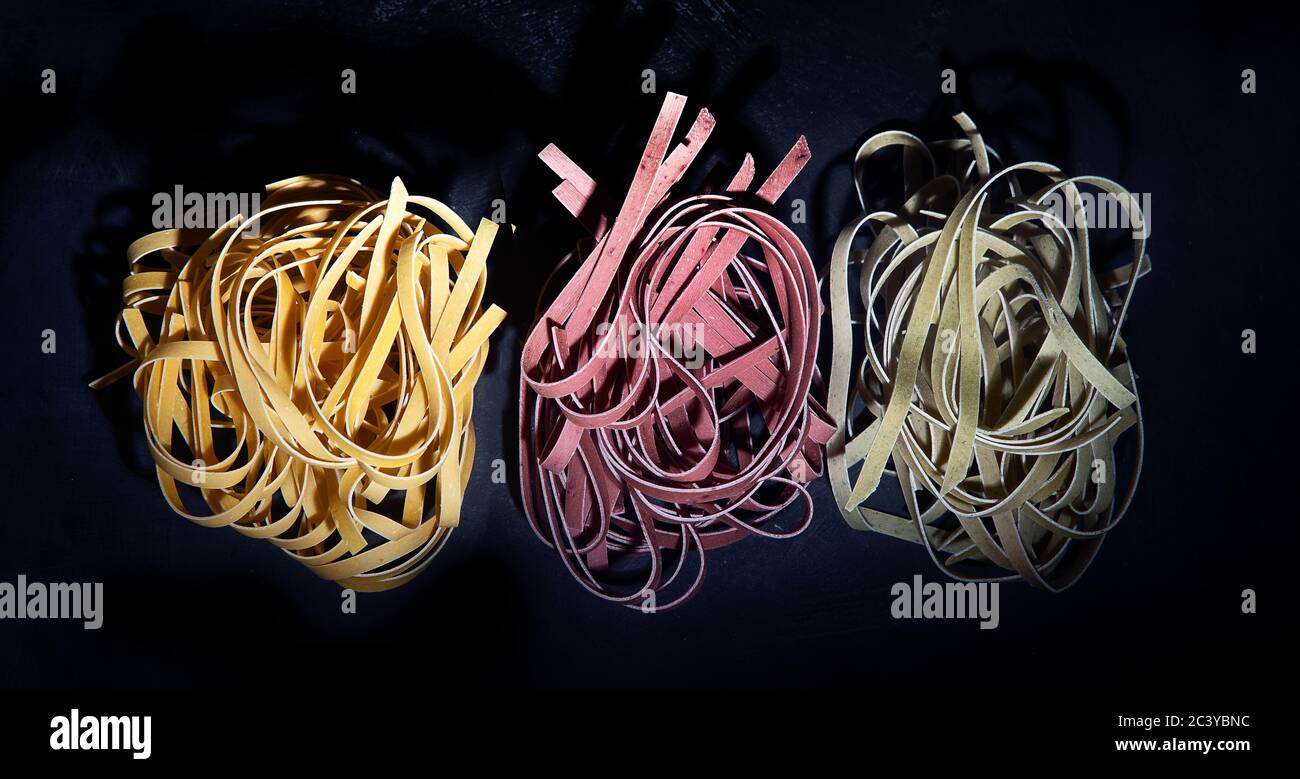 Italian raw uncooked tagliatelle pasta on black background. Top view ...