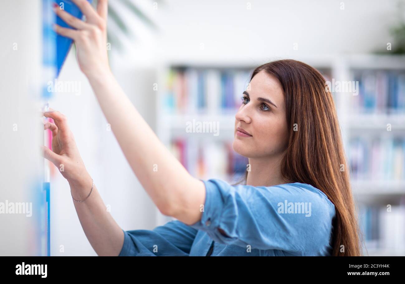 In the library - pretty female student with laptop and books working in ...