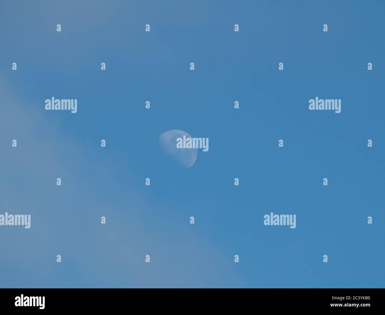 Day moon on blue sky with very light cloud in diagonal across bottom ...