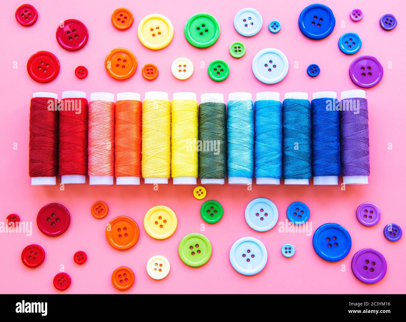 Spools of thread and buttons on the colors of the rainbow on a pink ...