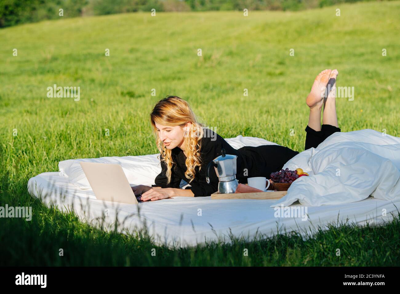 Woman enjoying working on laptop, lying in bed outdoors, under gentle ...