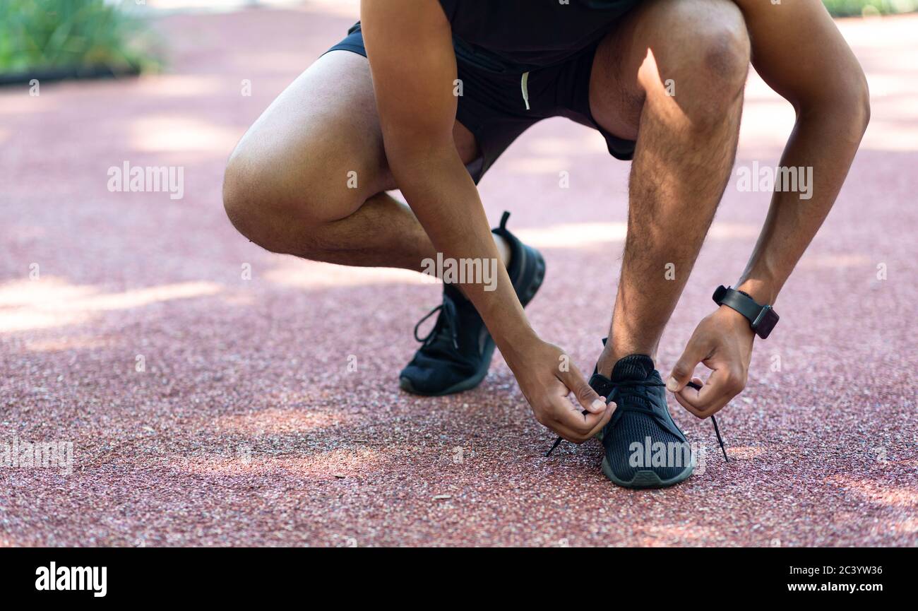 Closeup view of black jogger tying laces on his sports shoes during his ...