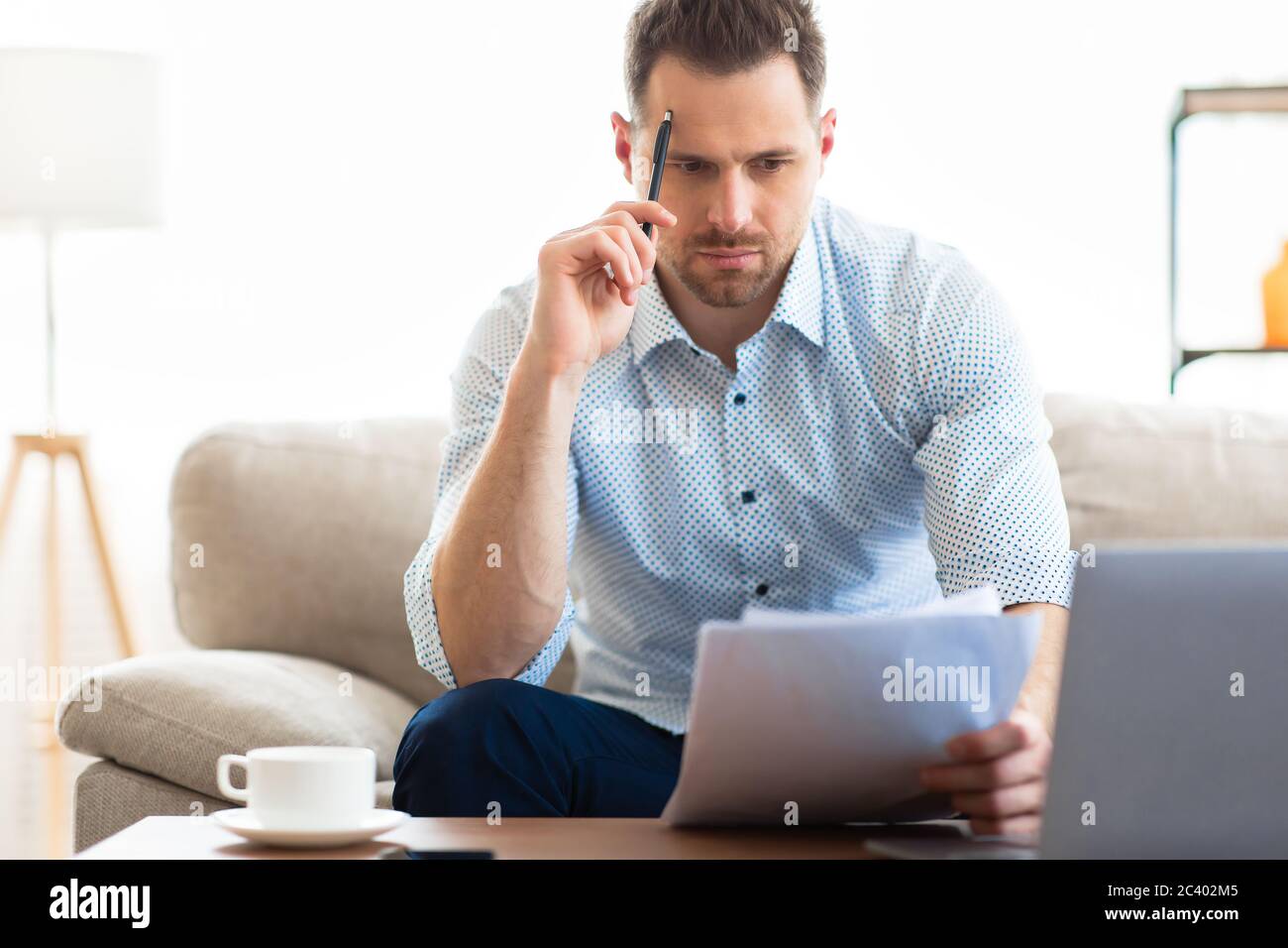 Pensive young man sitting at desk, looking at documents Stock Photo - Alamy