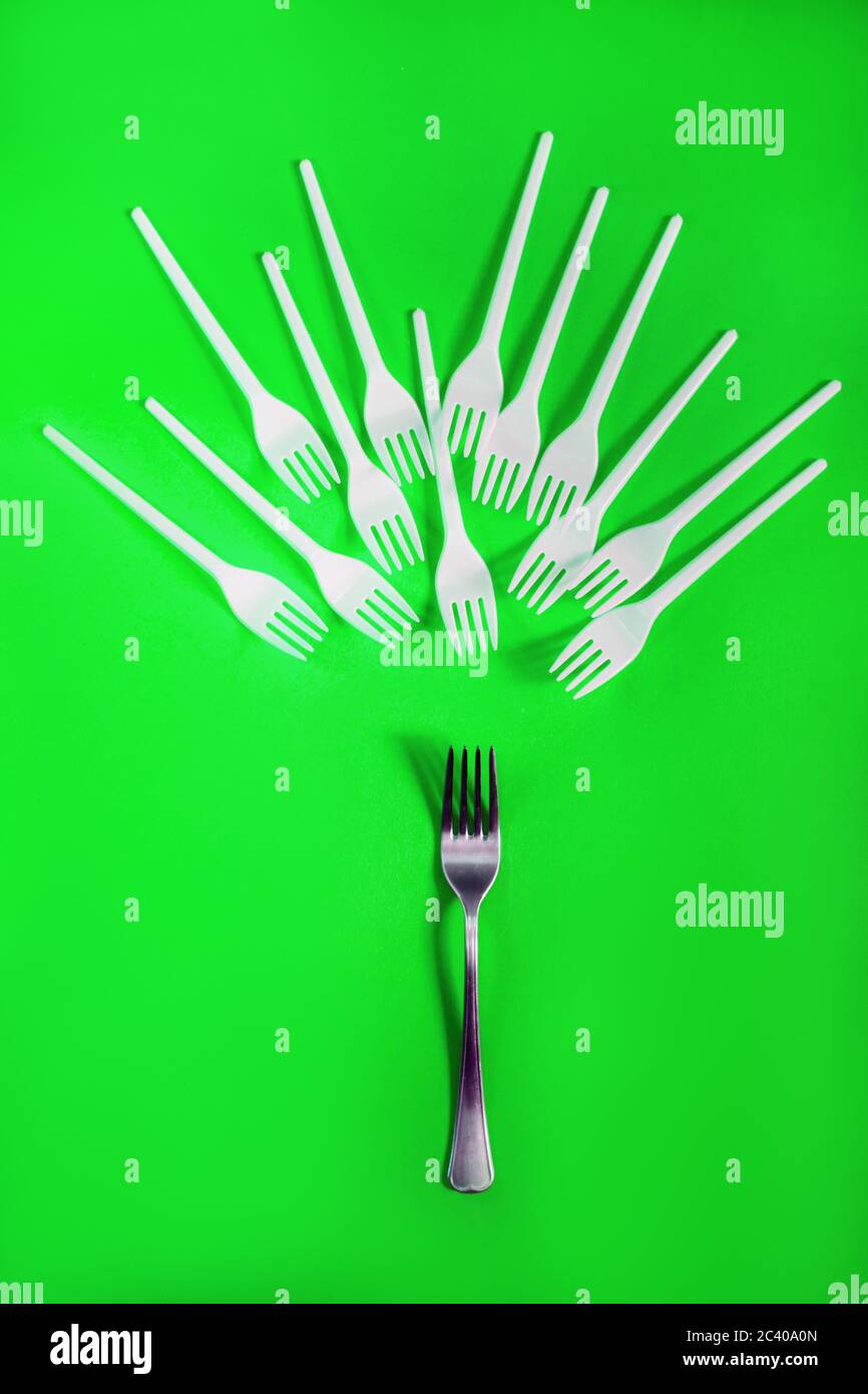 A lot of plastic forks vs one metal on a green background. The concept ...