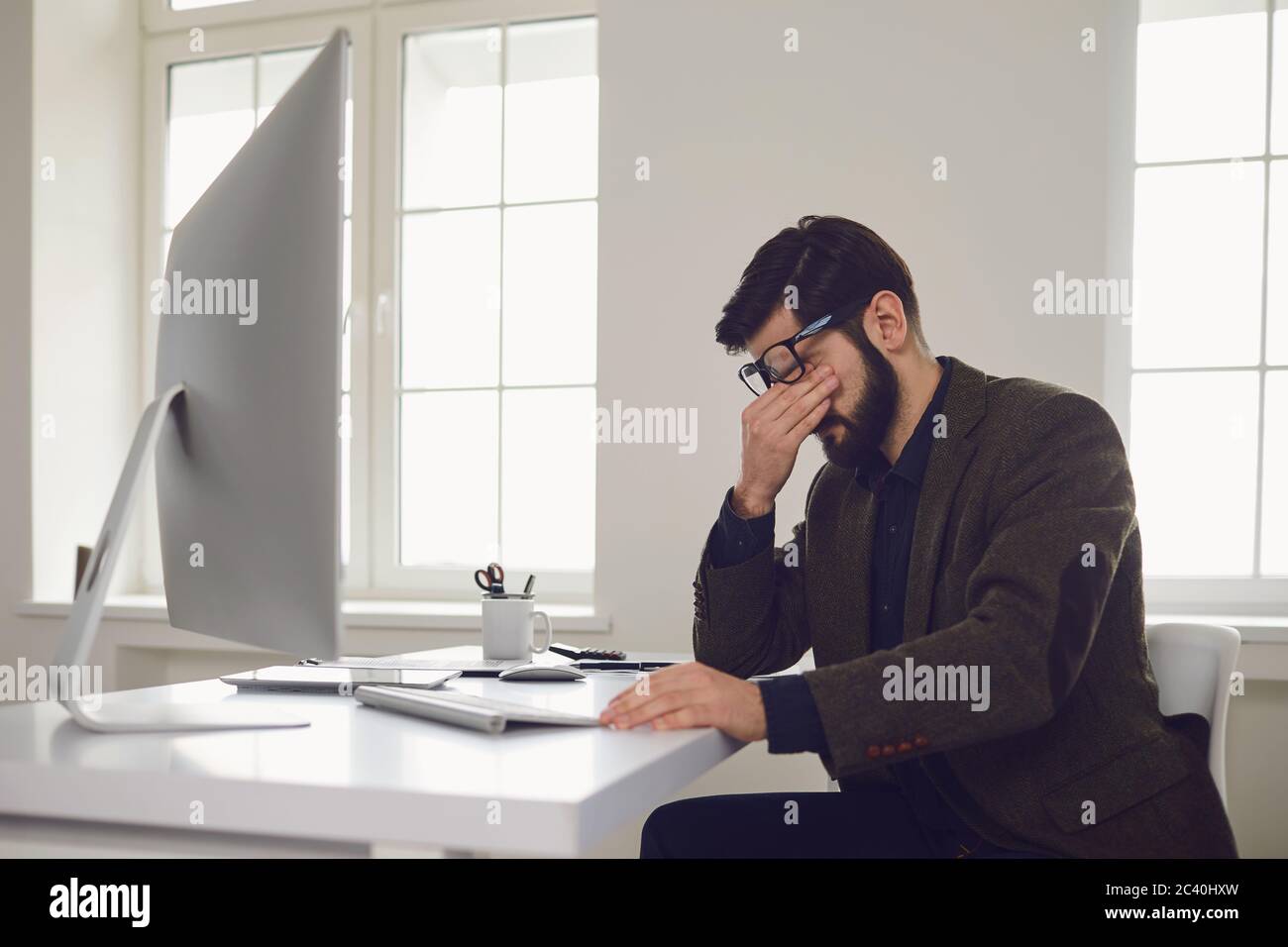 Exhausted tired worker at the workplace covered his face with his hands ...