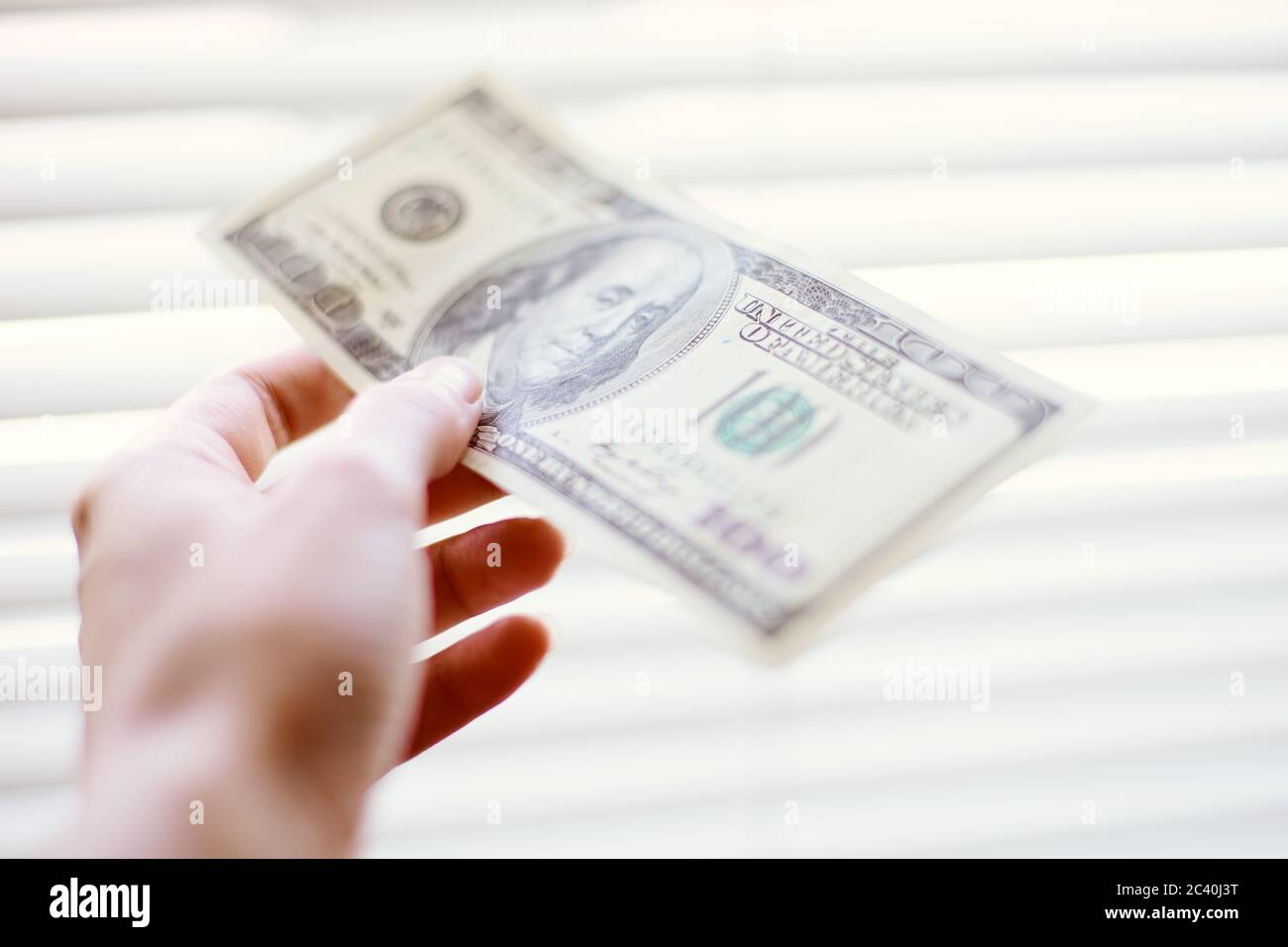 Hand with a 100 dollar bill on a background of white bright shutters ...