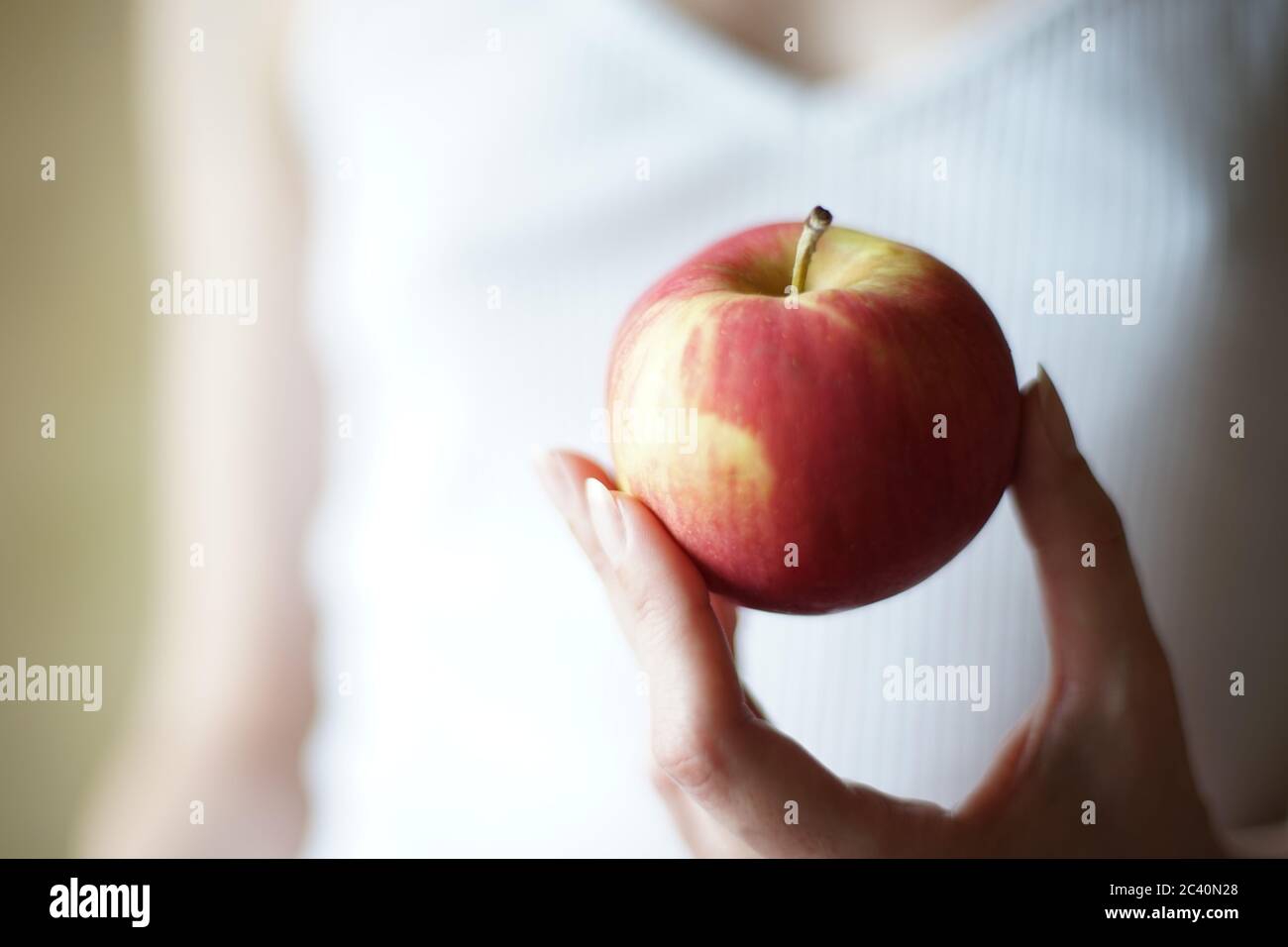 Red apple in female fingers on the background of a girl in a white ...