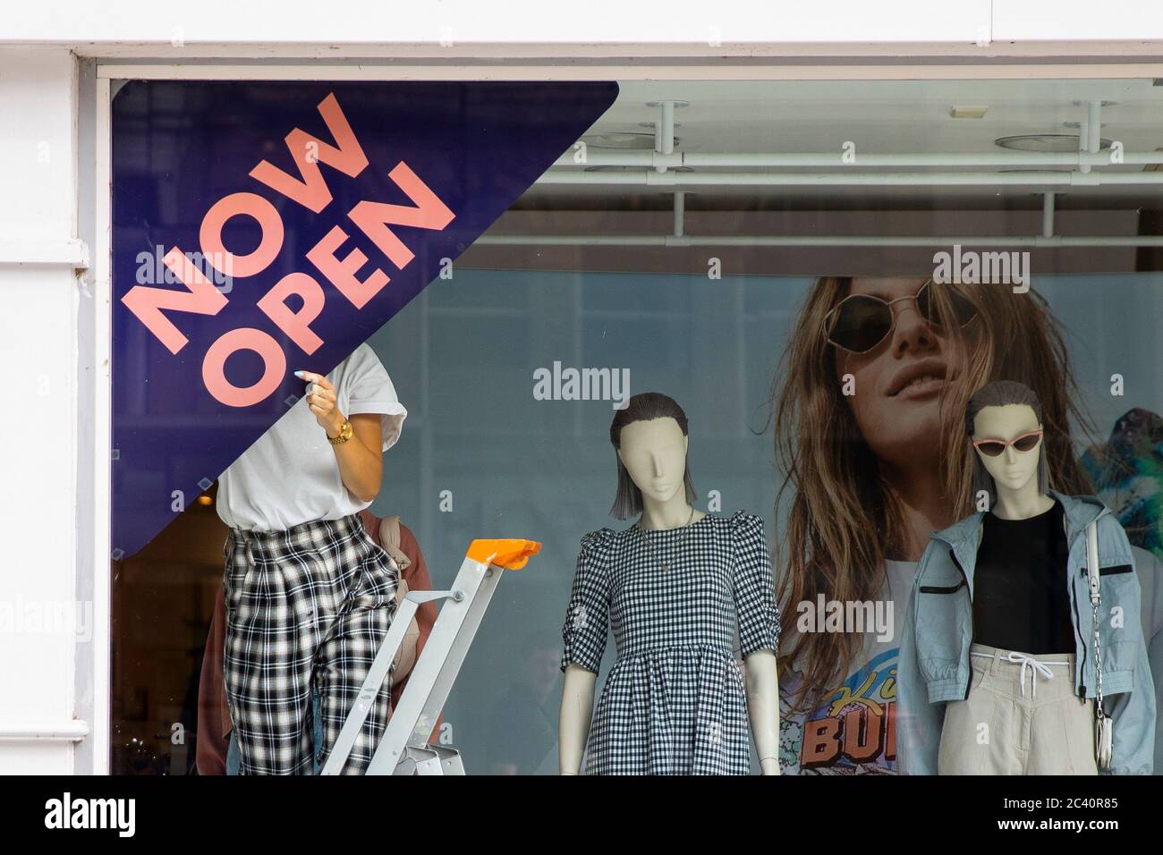 A shop worker arranges a shop window behind a ‘Now Open’ sign, 22nd ...